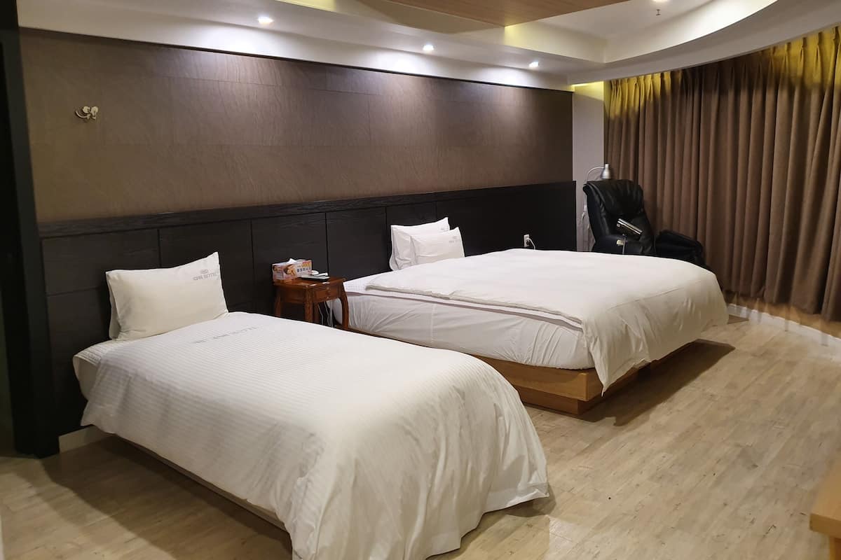 Quarto de hotel com duas camas, uma cabeceira de madeira, uma mesinha de cabeceira e uma cadeira.