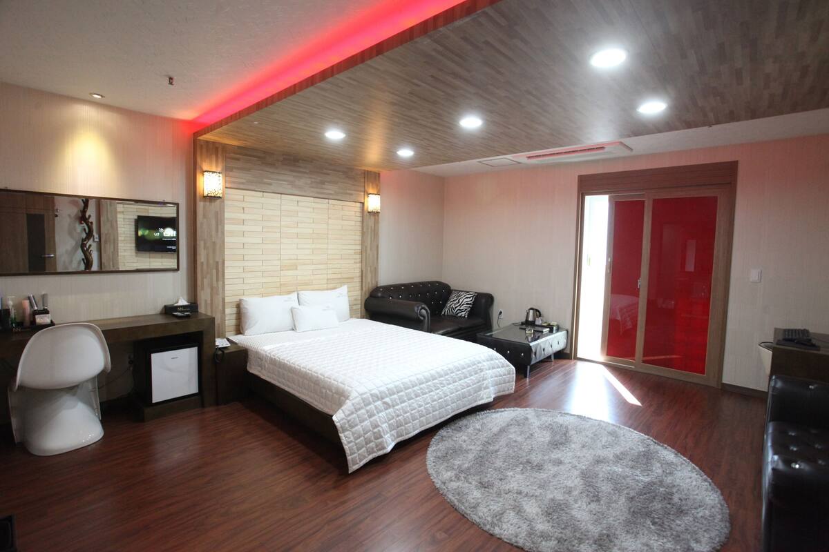 Um quarto moderno com uma cama, uma escrivaninha, uma cadeira e uma porta vermelha.