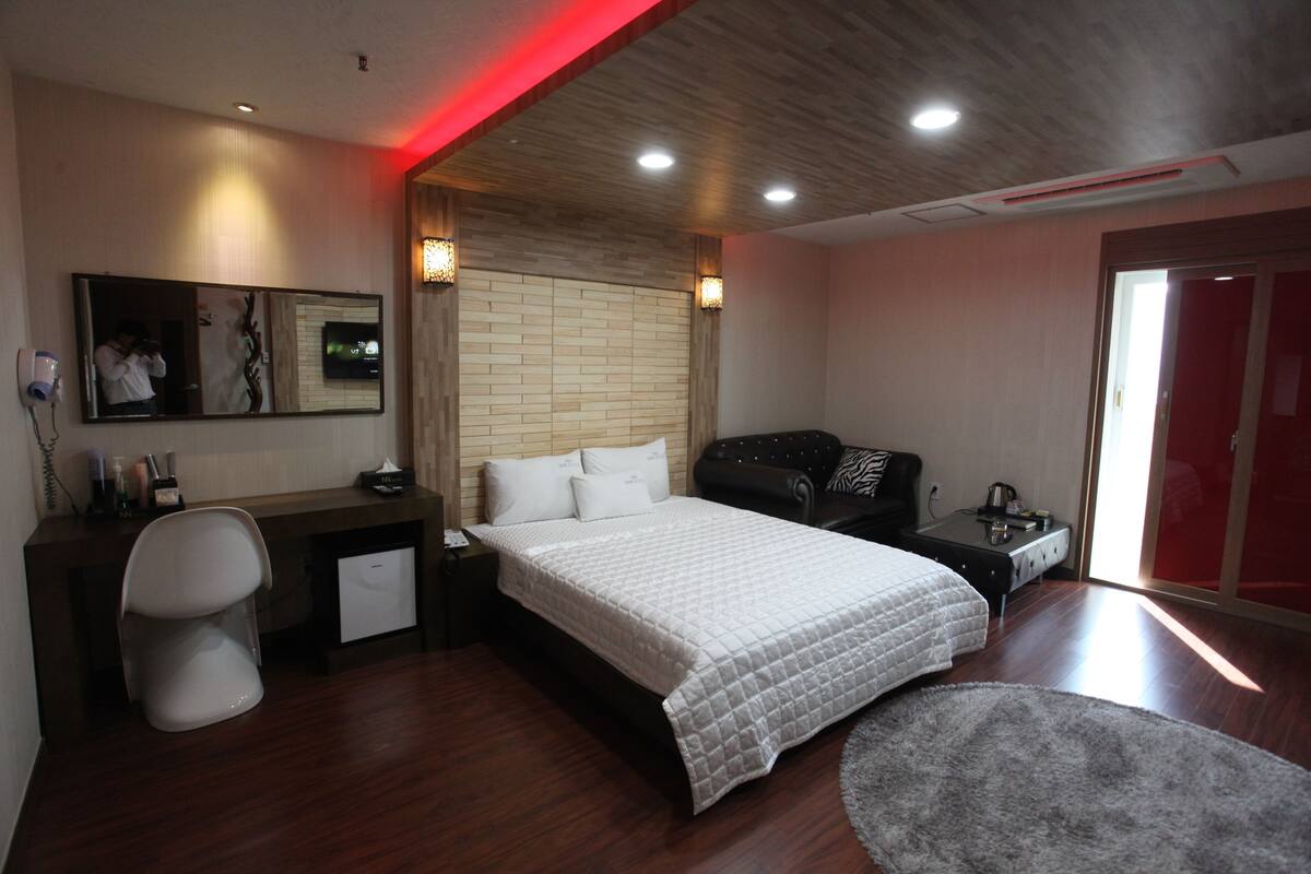 Quarto moderno com cama grande, escrivaninha, cadeira e televisão.