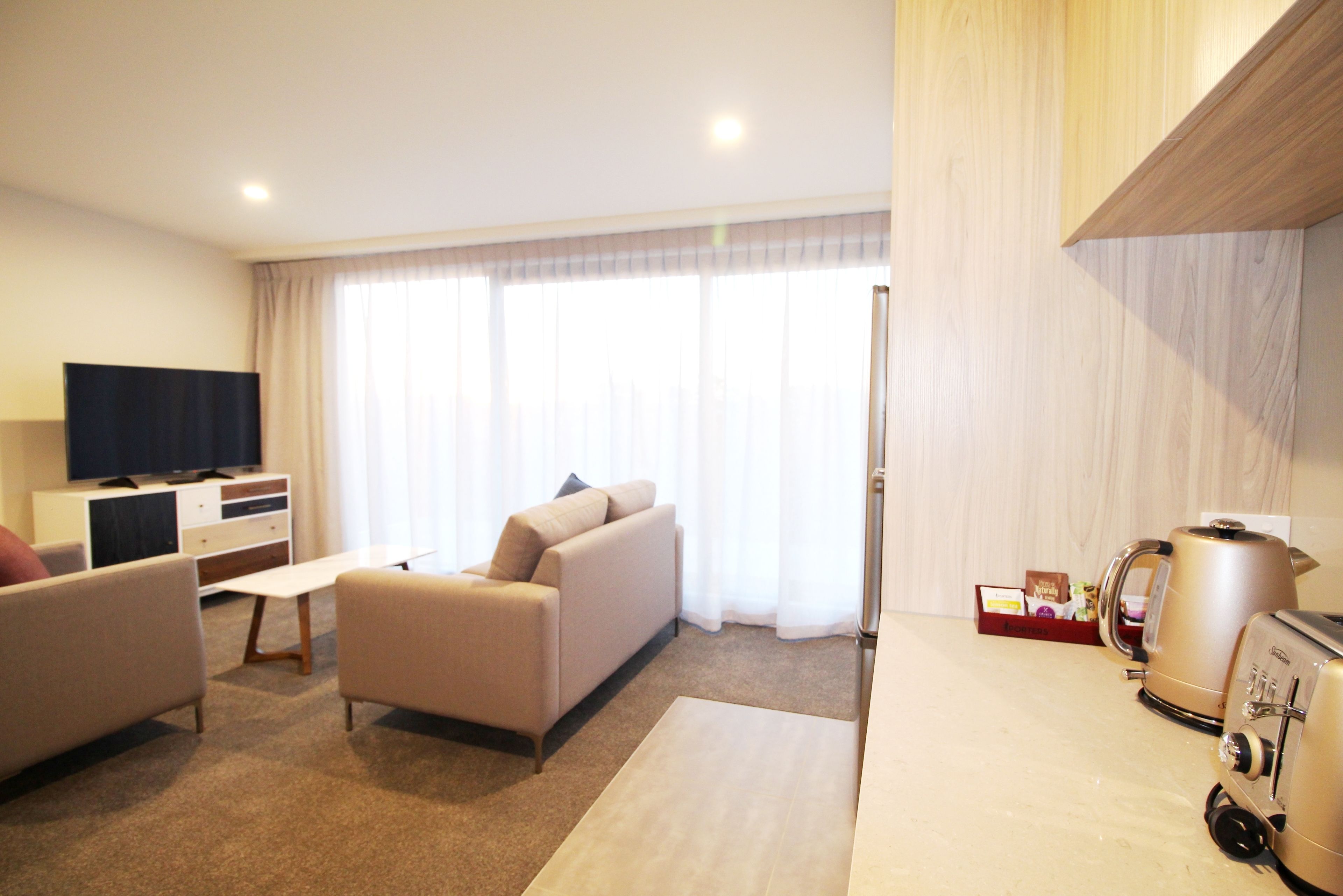 Quarto de hotel moderno com sofá, televisão, máquina de café e kitchenette.
