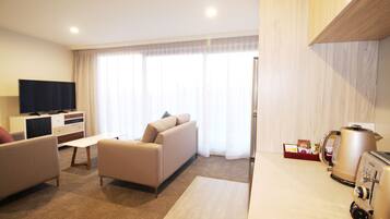 Quarto de hotel moderno com sofá, televisão, máquina de café e kitchenette.