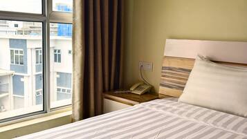 Quarto de hotel com uma cama, mesa de cabeceira com telefone, janela com cortinas e vista para edifícios.