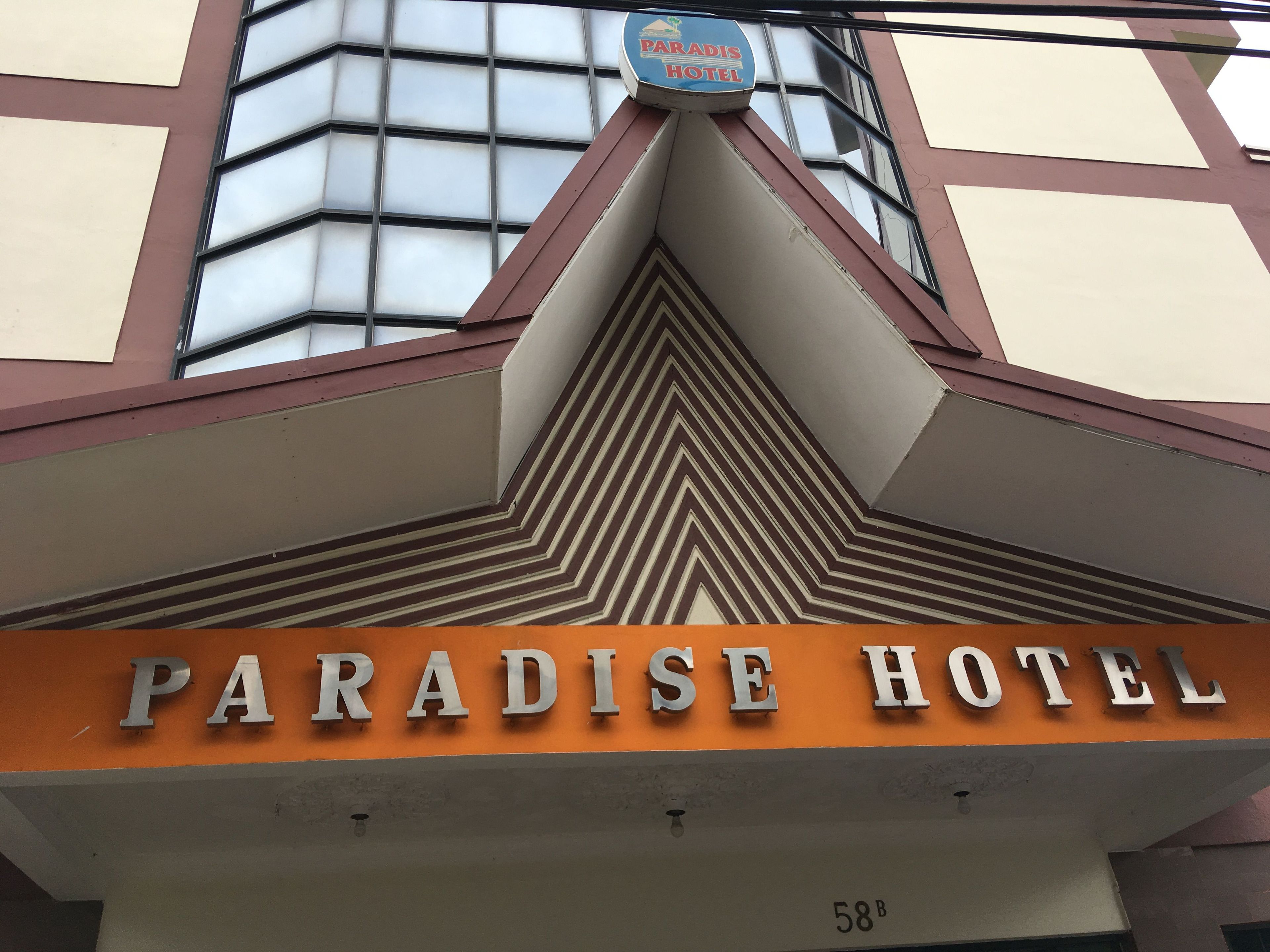 Exterior do Paradise Hotel, com uma placa em destaque e um design geométrico marcante.