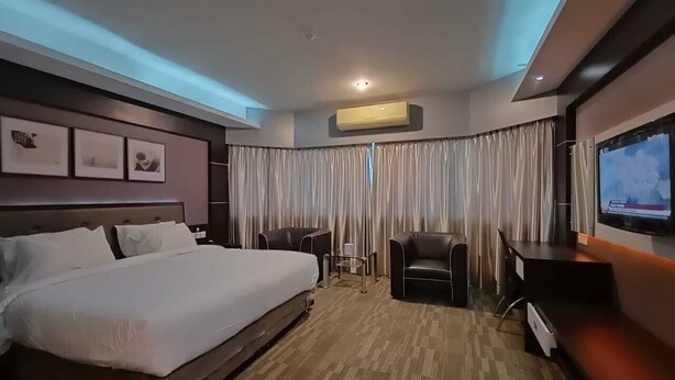 Quarto de hotel com uma cama grande, uma escrivaninha, uma cadeira, televisão e uma janela com cortinas.