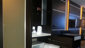 Quarto de hotel pequeno e funcional, com minibar, pia, espelho e televisão.