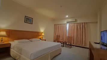 Quarto de hotel com uma cama grande, duas mesas de cabeceira com luminárias, uma escrivaninha com computador e uma janela com cortinas.