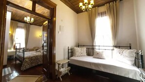 Quarto com cama grande, vigas de madeira no teto, um candelabro e vista para outro cômodo.