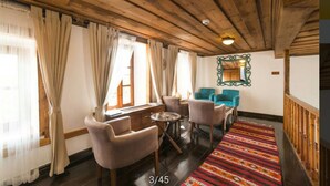 Quarto aconchegante com vigas de madeira, um piano, duas cadeiras e um tapete estampado.
