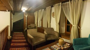 Um quarto aconchegante com uma escada, dois poltronas, uma mesa com revistas e uma chaleira, e uma janela com cortinas.