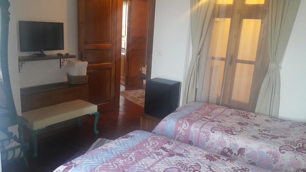 Quarto com cama, um banquinho, televisão e um aparelho de som.