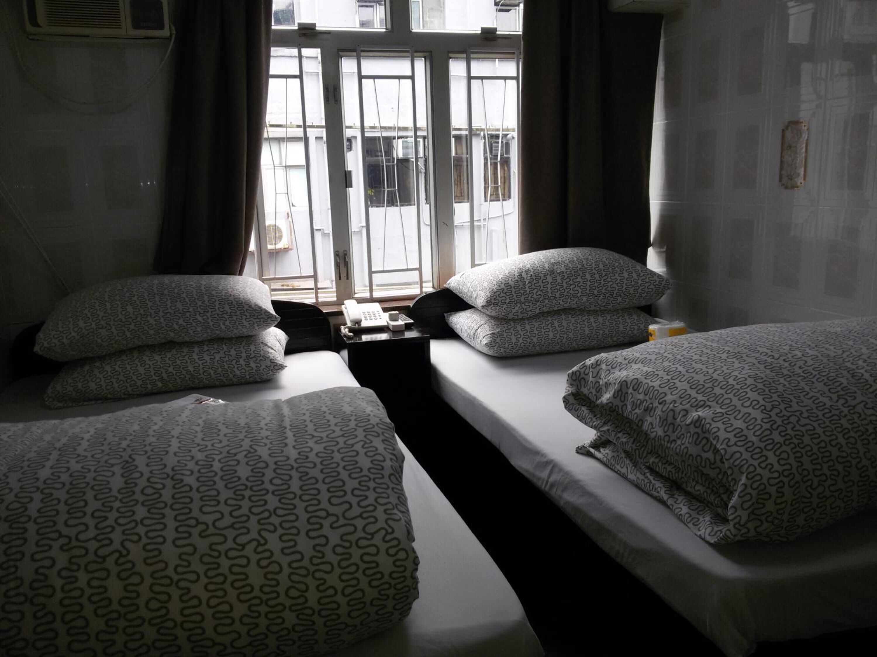 Quarto de hotel com duas camas, cada uma com roupa de cama estampada, mesa de cabeceira com telefone e janela com cortinas.
