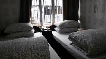 Quarto de hotel com duas camas, cada uma com roupa de cama estampada, mesa de cabeceira com telefone e janela com cortinas.