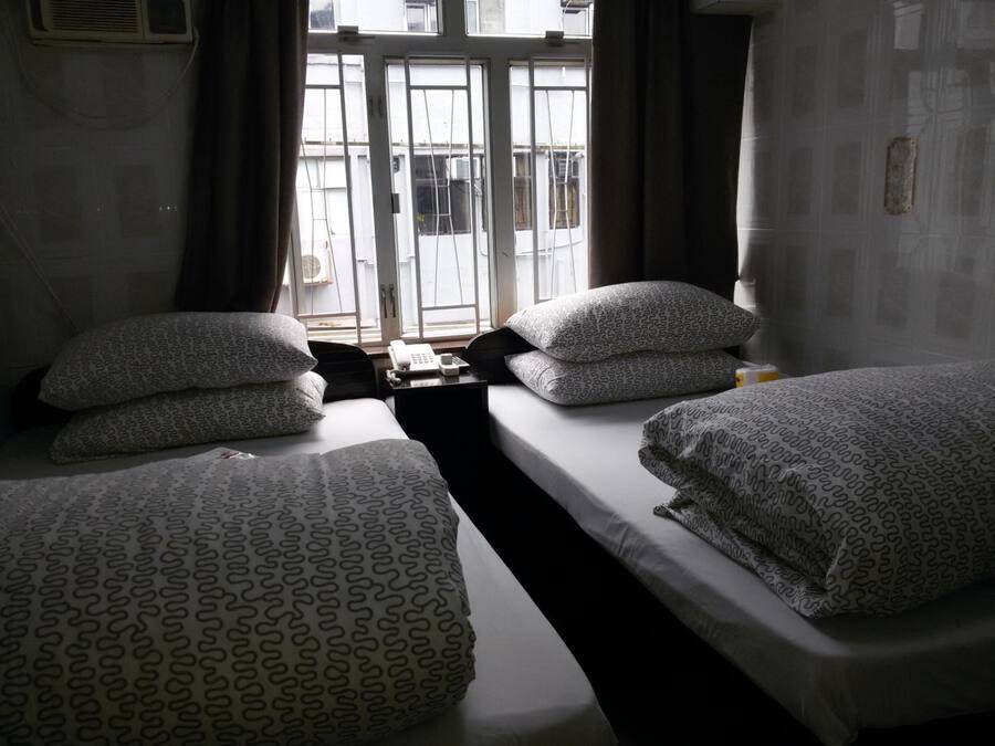 Quarto de hotel com duas camas, cada uma com roupa de cama estampada, mesa de cabeceira com telefone e janela com cortinas.