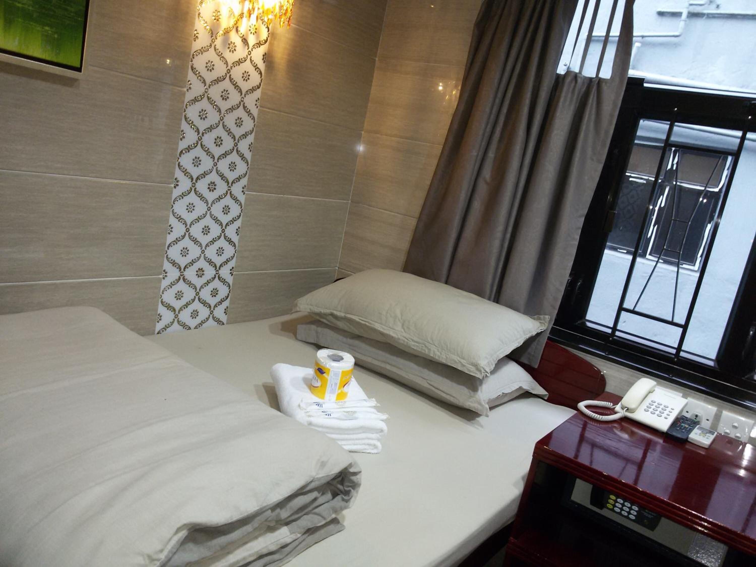 Quarto de hotel com cama, telefone ao lado e janela com cortinas.