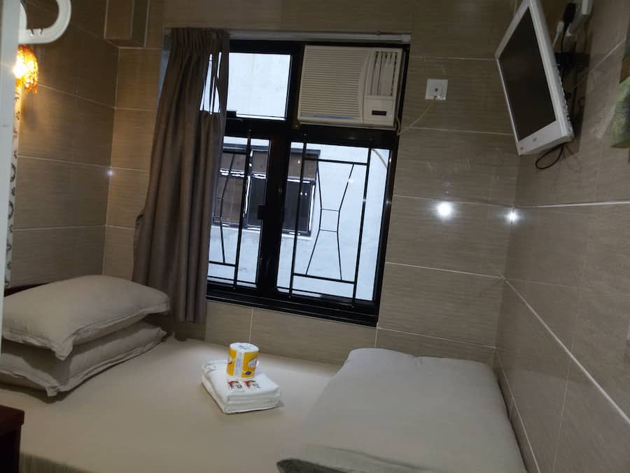 Quarto de hotel com cama, janela com cortinas, ar condicionado e televisão fixada na parede.