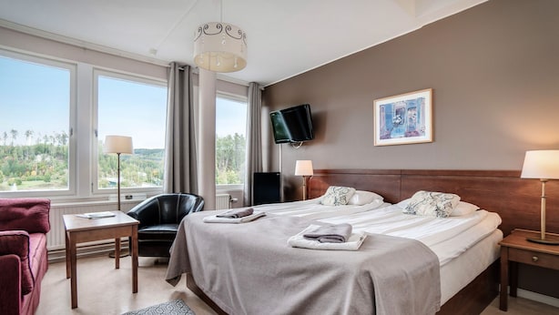 Quarto de hotel com uma cama grande, escrivaninha, cadeira, televisão e vista para o exterior.