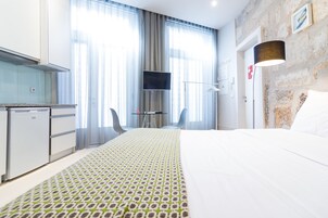 Quarto de hotel com cama, mesa de trabalho, cadeira, televisão e cozinha compacta.
