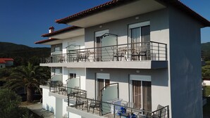 Um edifício de dois andares com varandas, móveis de exterior e um carro estacionado nas proximidades.
