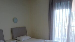 Quarto de hotel com duas camas, uma mesa pequena e uma janela com cortinas.