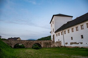 Uma ponte de pedra, um edifício branco com uma torre e uma área gramada.
