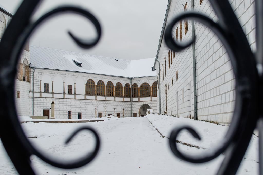 Pátio coberto de neve com um edifício branco, com janelas em arco e um arco central.