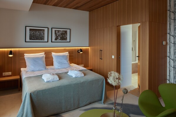 Quarto de hotel moderno com uma cama grande, cabeceira de madeira, duas fotos emolduradas na parede e uma cadeira verde.
