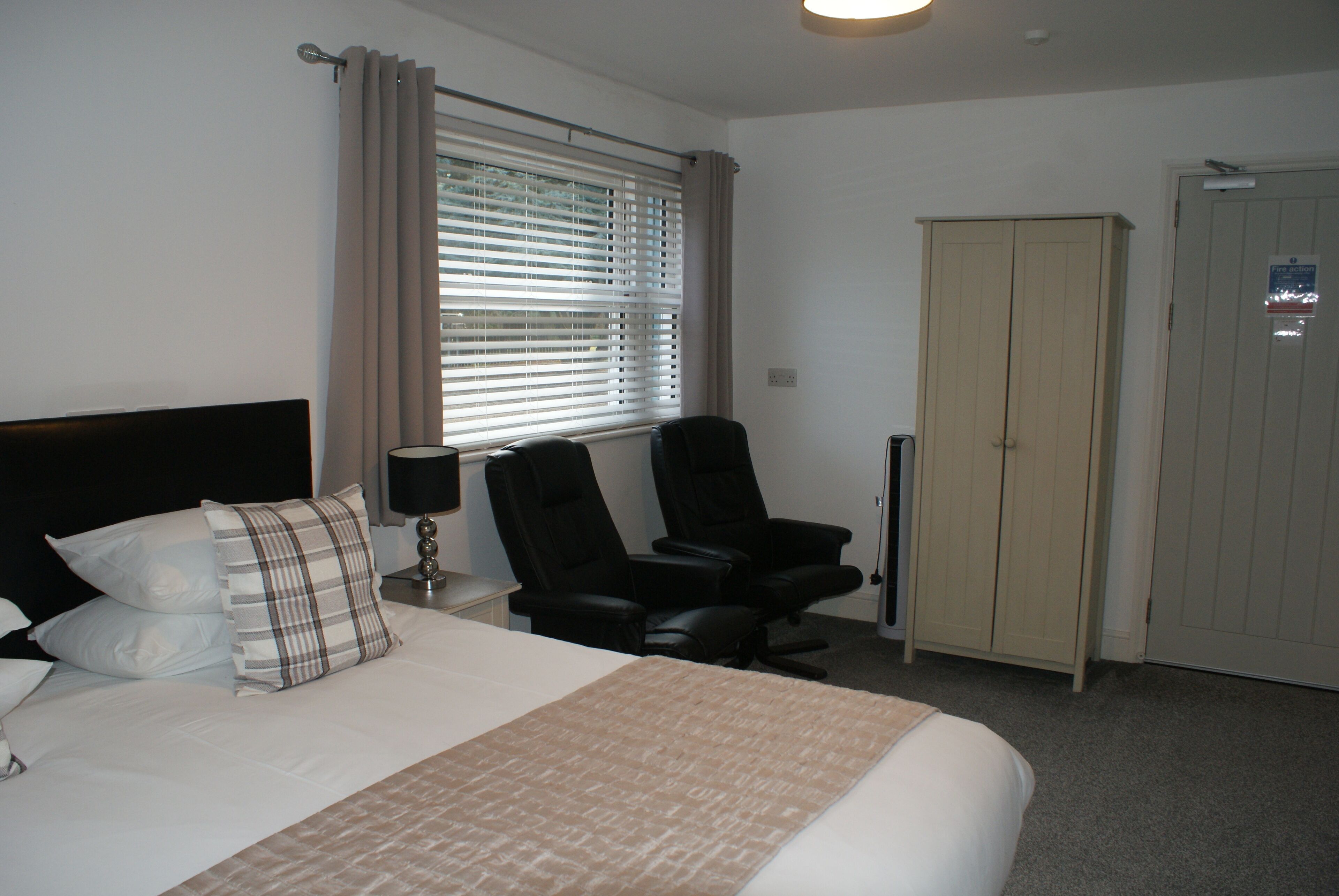 Quarto de hotel com cama, duas cadeiras, guarda-roupa e janela com cortinas.