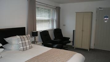Quarto de hotel com cama, duas cadeiras, guarda-roupa e janela com cortinas.