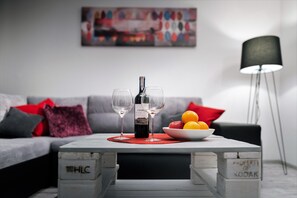 Uma sala de estar moderna com uma mesa de centro branca, duas taças de vinho, uma garrafa de vinho e uma cesta de frutas.