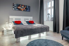 Quarto moderno com cama, mesas de cabeceira, escrivaninha e janela com cortinas.