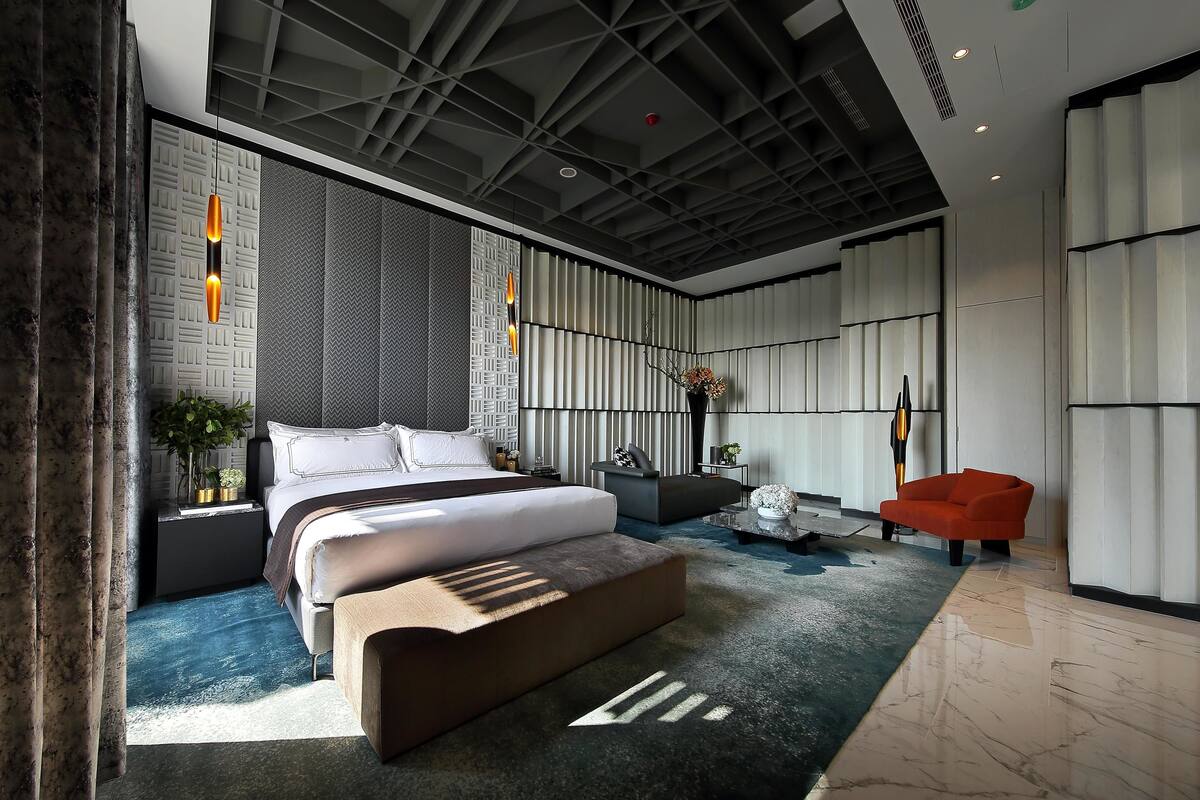 Quarto moderno com uma cama grande, um sofá, uma poltrona vermelha e um painel decorativo na parede.
