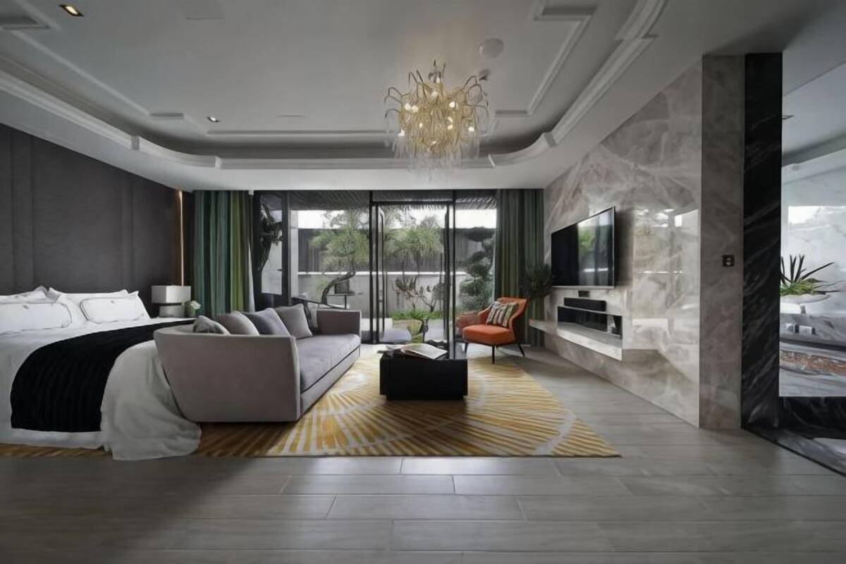 Quarto moderno com cama, sofá, TV e vista através de grandes janelas.