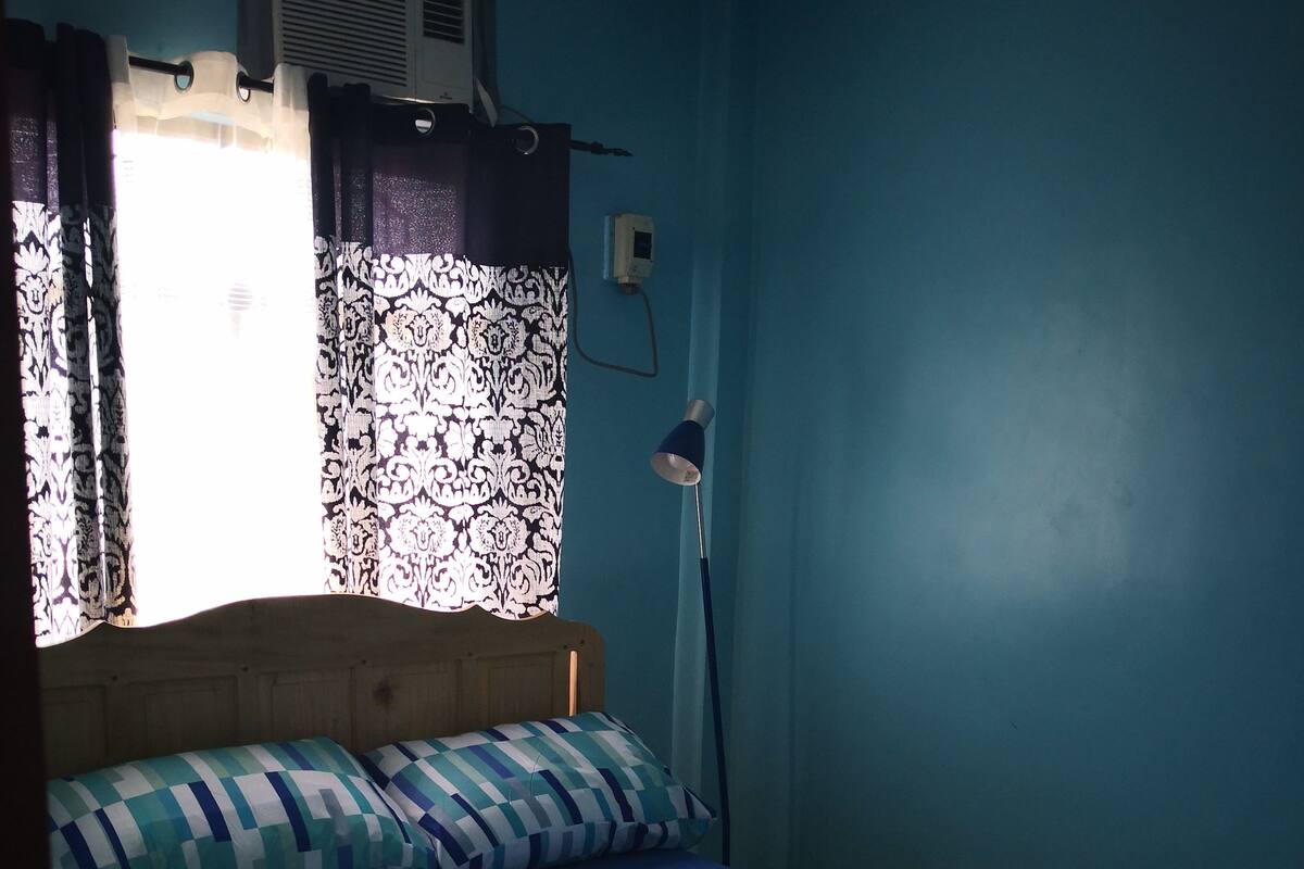 Um quarto com cama, cortinas, abajur e ar condicionado.
