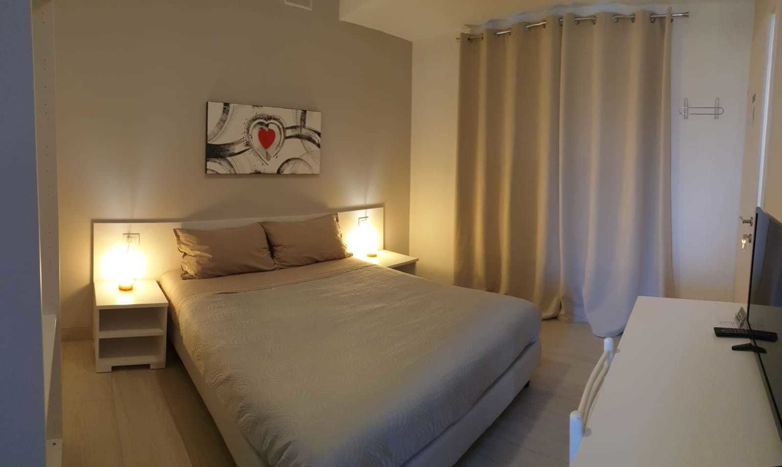 Um quarto com cama, mesas de cabeceira, televisão e um quadro na parede.