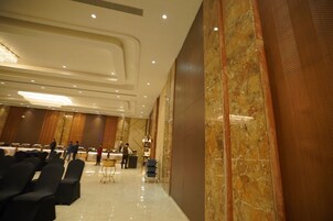 Uma sala de conferências espaçosa com fileiras de cadeiras, um painel de mármore e uma área de recepção com funcionários.
