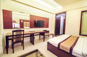 Quarto de hotel com cama, escrivaninha, cadeira, televisão fixada na parede e espelho.