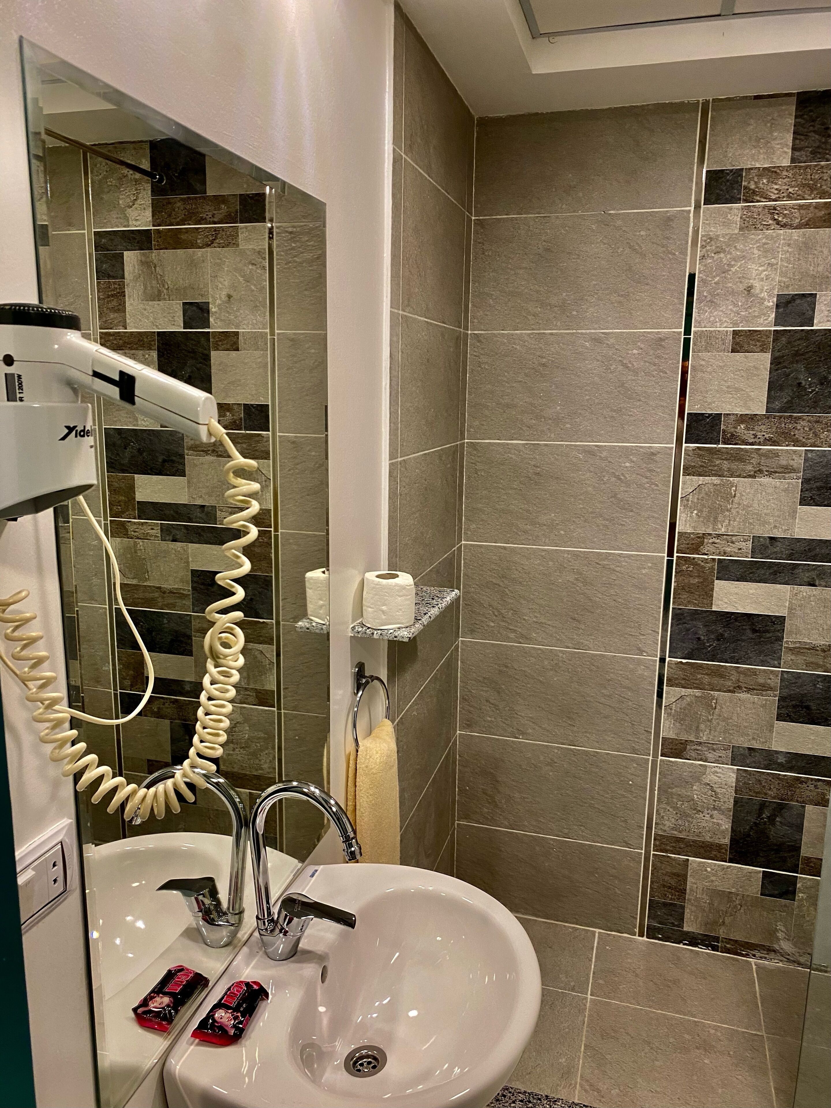Casa de banho com lavatório branco, secador de cabelo e zona de duche.