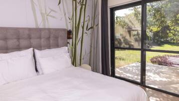 Quarto com uma cama grande, janela e vista para um jardim.