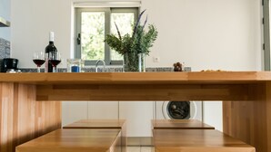 Uma cozinha com bancada de madeira, dois copos de vinho tinto, uma garrafa de vinho e um vaso com plantas verdes.