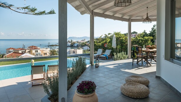 Uma área externa coberta com piscina, espreguiçadeiras e vista para o mar.