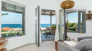 Sala moderna com uma janela ampla que oferece vista para o mar e uma varanda com mobiliário de exterior.