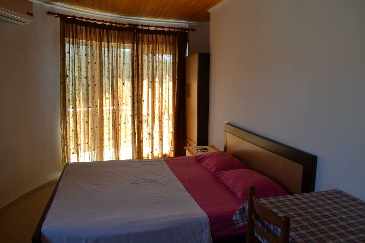 Quarto com cama, mesa de cabeceira, mesa e cadeira.