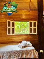 Um quarto de madeira com uma cama, uma janela com persianas e o logotipo da 'Hilamito Lodge'.