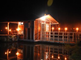 Uma cabana de madeira com varanda, um pequeno alpendre e um reflexo na água.