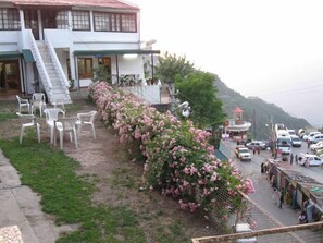 Um edifício com escadaria que leva a um alpendre, rodeado por um jardim cheio de flores cor-de-rosa.