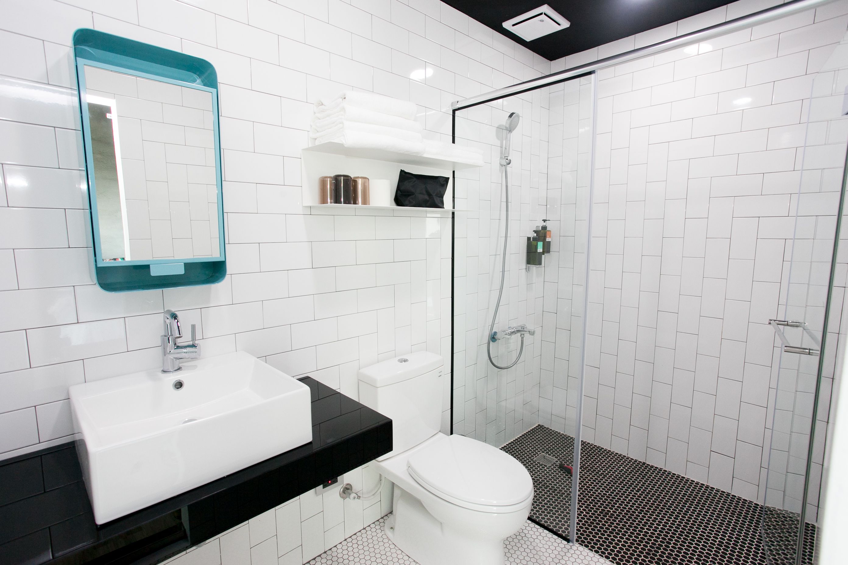 Casa de banho moderna com lavatório branco, bancada preta e cabine de duche em vidro.