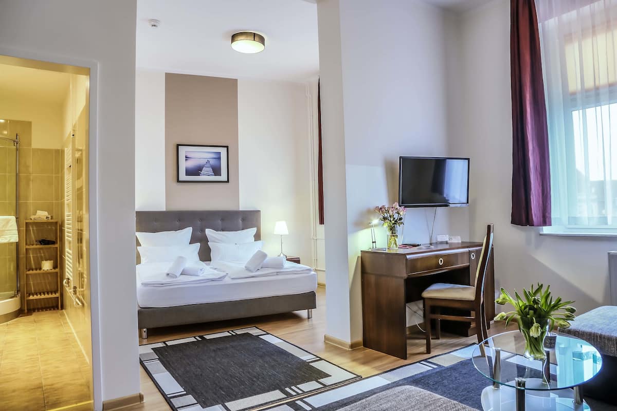 Quarto de hotel com cama, escrivaninha, cadeira, televisão e banheiro com chuveiro e vaso sanitário.