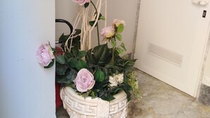Planta em vaso com flores e galhos rosa, junto a uma parede e uma porta com um aviso.
