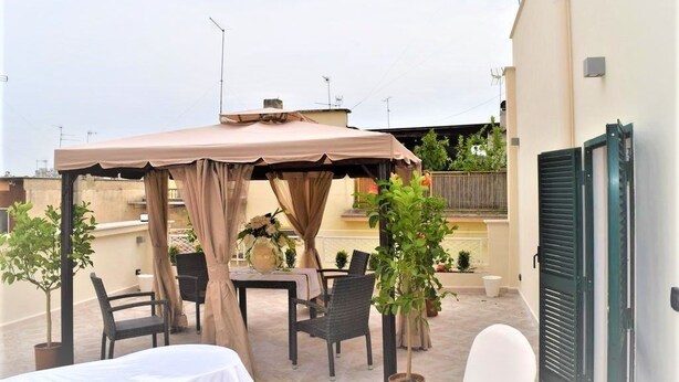 Terraço no telhado com área de estar coberta, cadeiras, mesa e plantas em vasos.