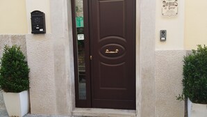 Uma porta marrom com puxador de latão, uma placa em cima e dois vasos de plantas de cada lado.